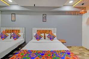 Quarto de hotel com duas camas, cabeceira de madeira, colcha com padrão geométrico colorido e luminária pendente.