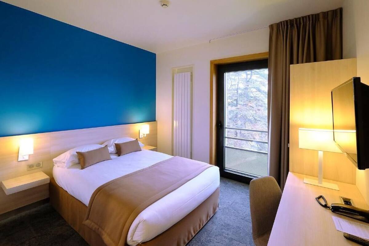 Quarto de hotel com uma cama grande, mesas de cabeceira, uma escrivaninha com abajur e uma televisão.