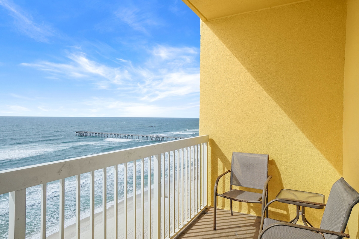 Varanda com vista para o oceano e um cais, com duas cadeiras e uma mesa.