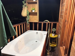 Casa de banho exterior privada com banheira, chuveiro dourado e uma pequena planta em vaso.