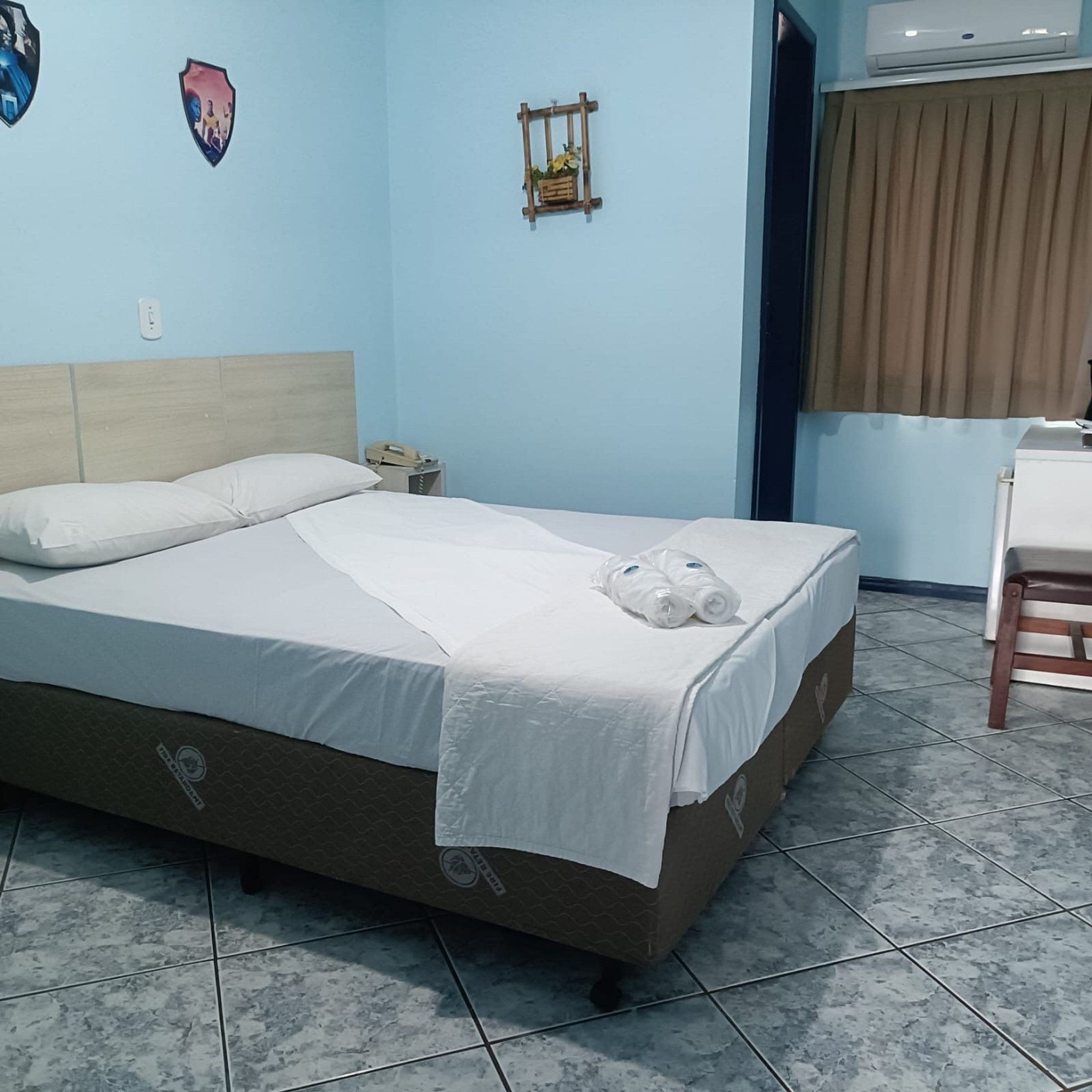 Uma cama com lençóis brancos, cabeceira de madeira e uma pequena mesa de cabeceira com abajur.