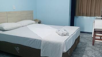 Uma cama com lençóis brancos, cabeceira de madeira e uma pequena mesa de cabeceira com abajur.