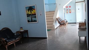 Quarto com cadeira de madeira, uma pequena mesa, um quadro na parede e escada que leva a outra área.