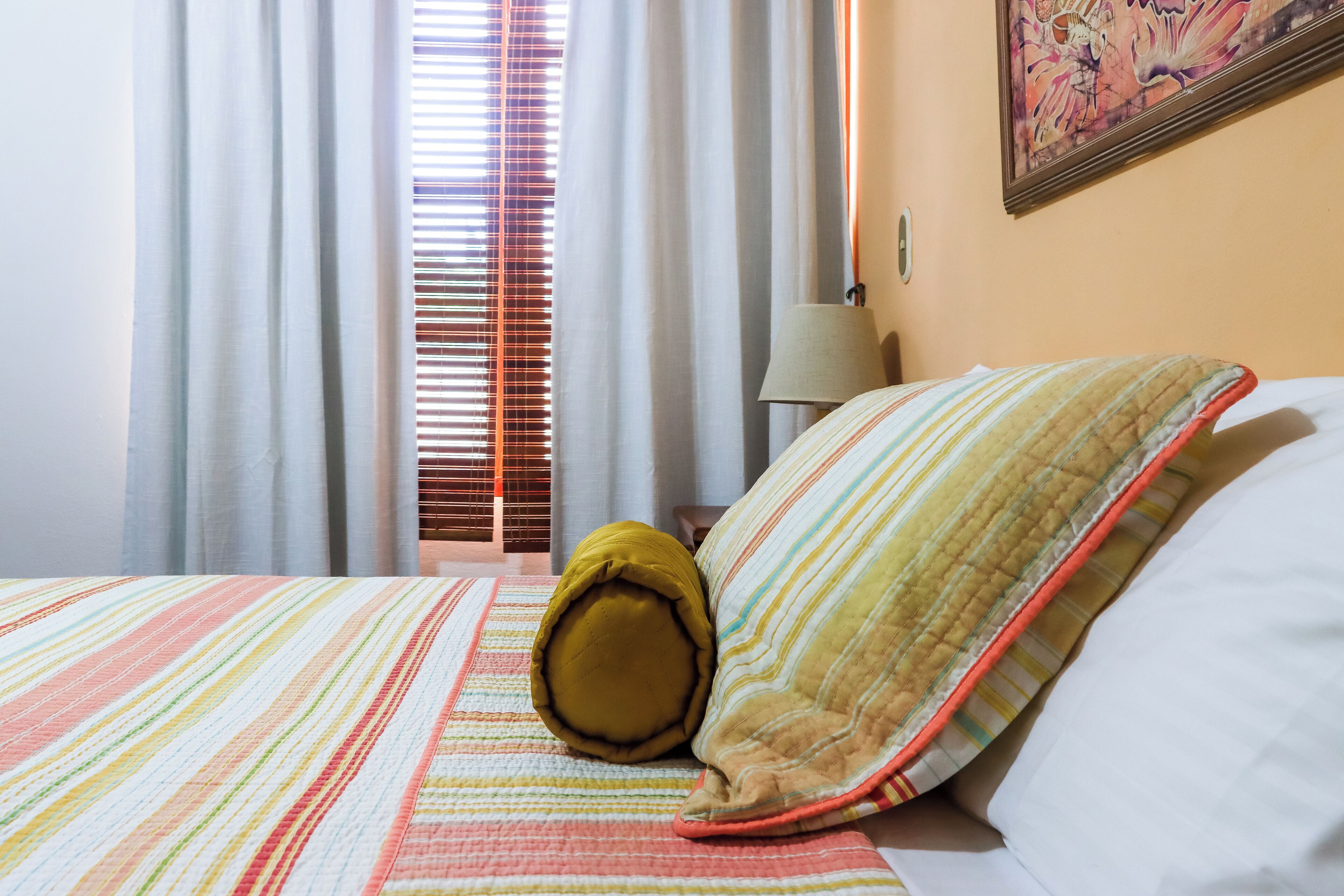 Uma cama com roupa de cama listrada, um travesseiro, uma luminária e uma janela com persianas.