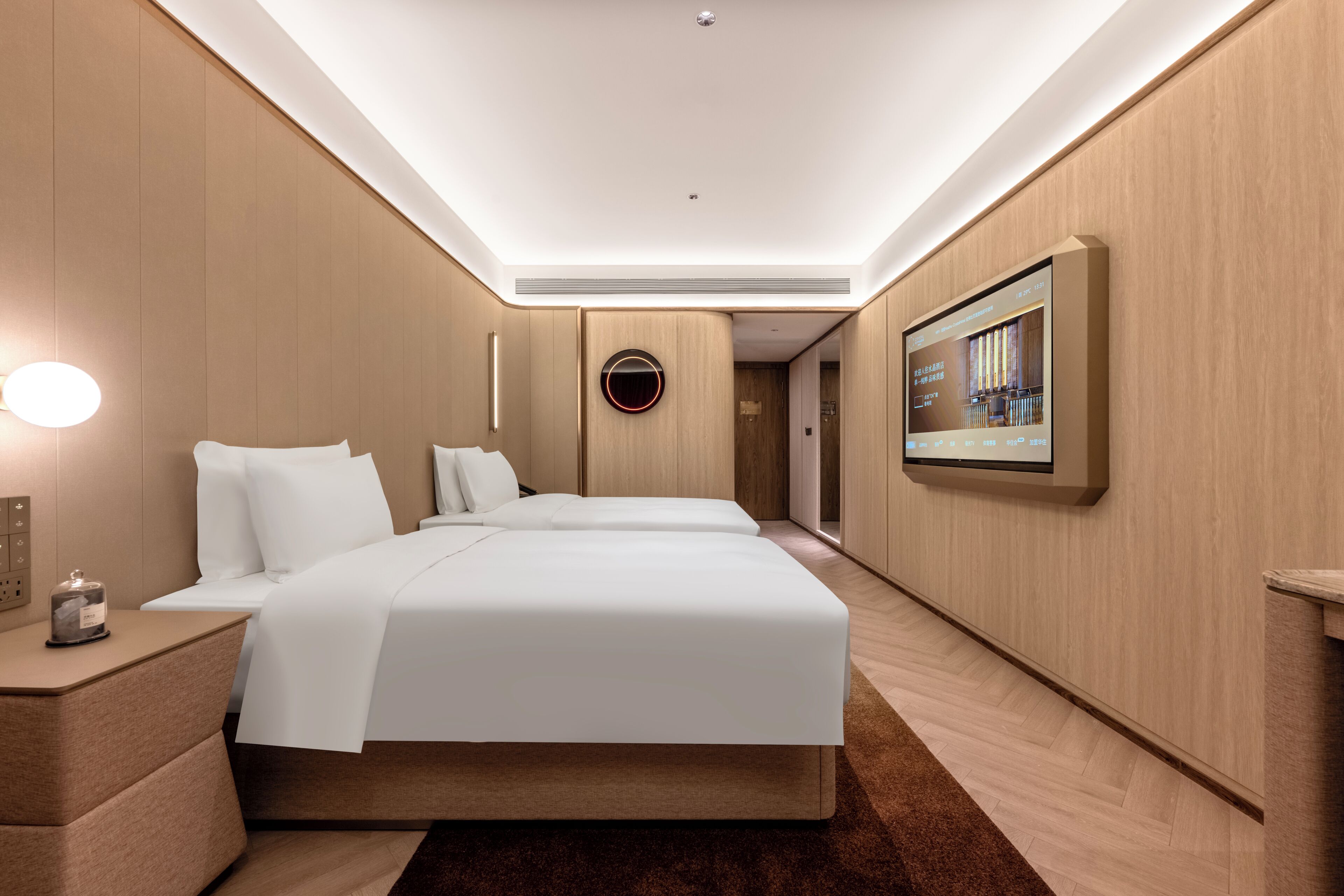 Quarto de hotel moderno com uma cama grande, mesa de cabeceira, televisão na parede e luminária no teto.