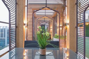 Mesa de vidro com um vaso trançado de plantas verdes, guarda-corpo de metal e vista de edifícios através de um painel decorado.