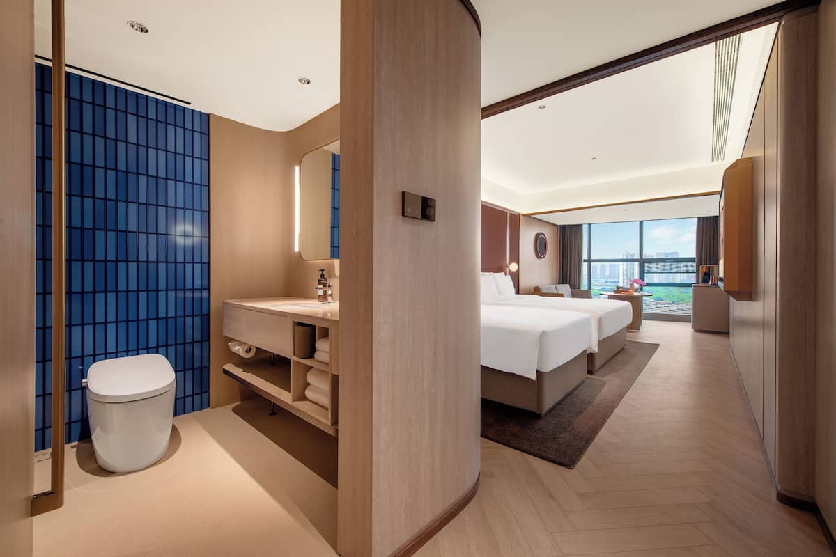 Quarto de hotel moderno com uma cama grande, banheiro com azulejos azuis e vista para a cidade.