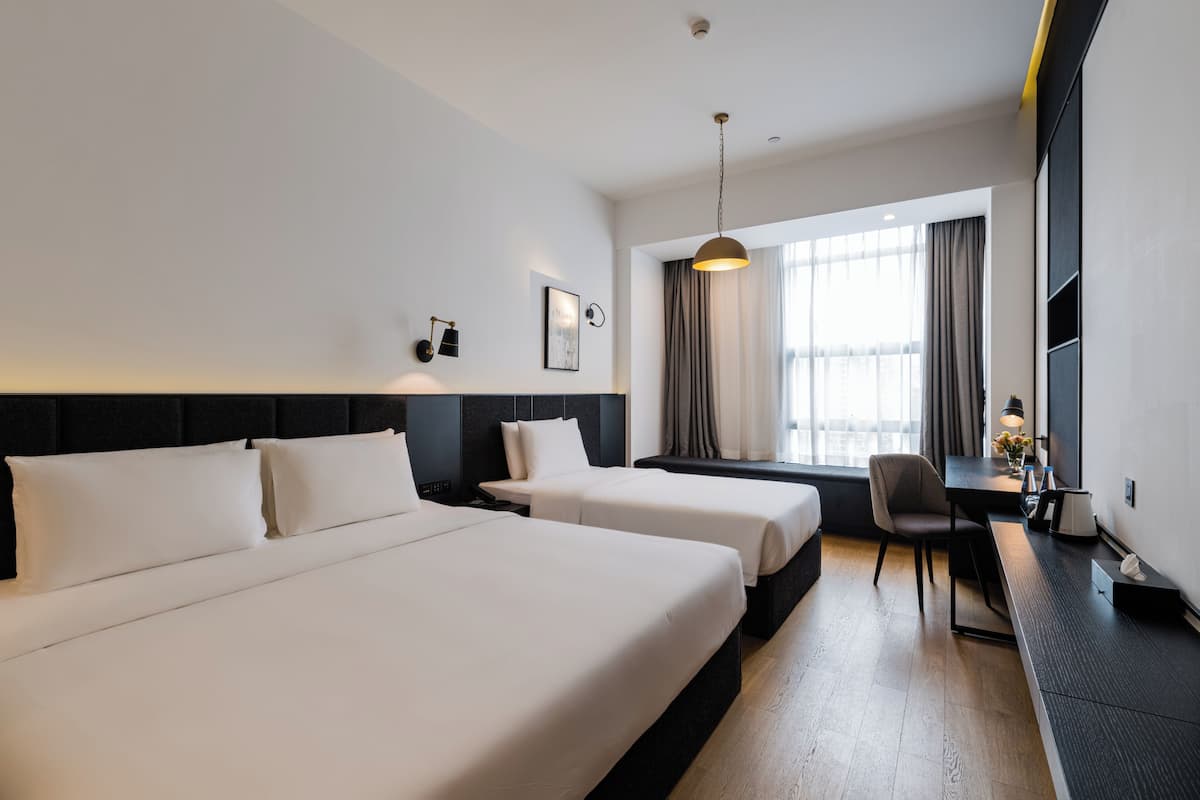Quarto de hotel com duas camas, uma escrivaninha, uma cadeira, uma televisão e uma janela com cortinas.