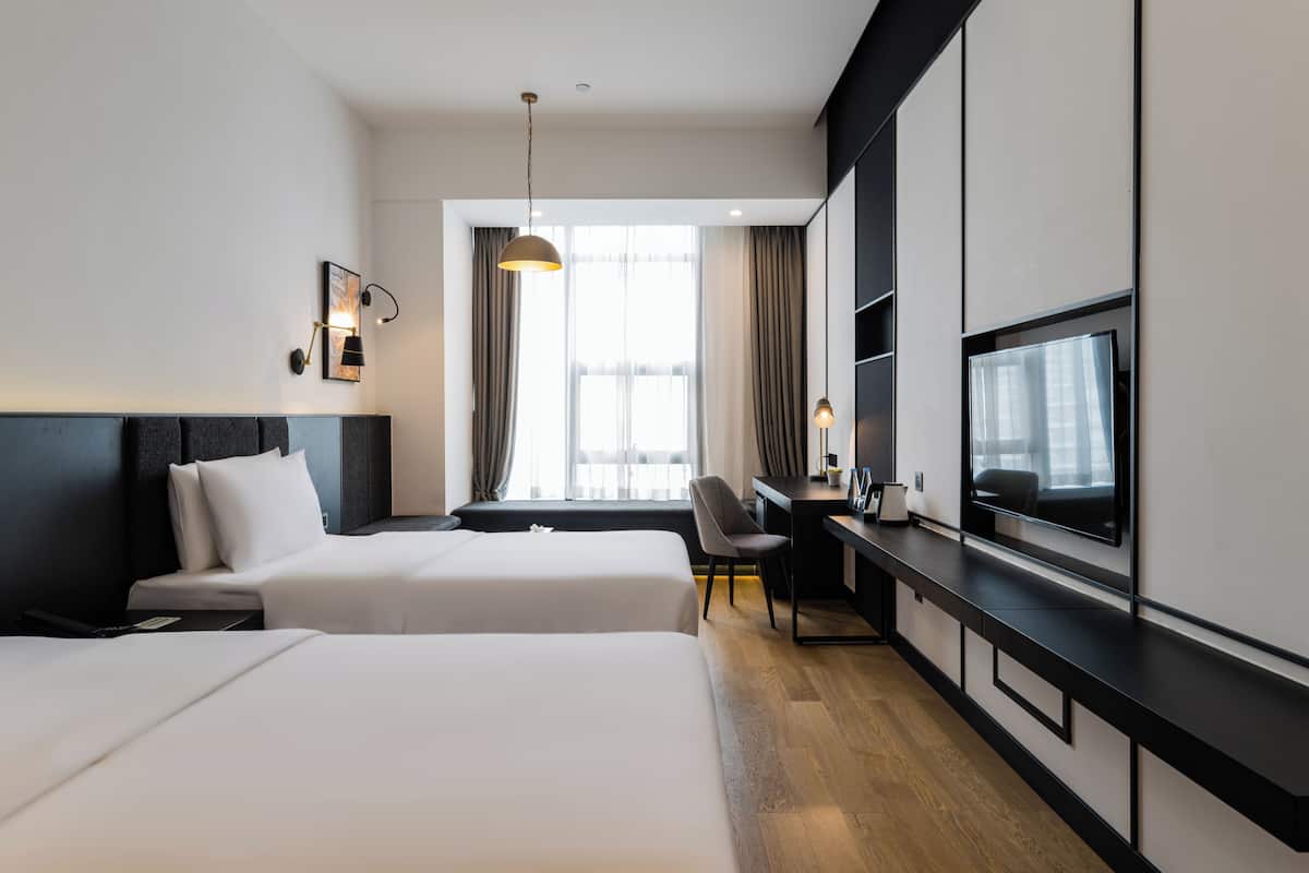 Quarto de hotel com duas camas, uma escrivaninha, televisão e janela com cortinas.