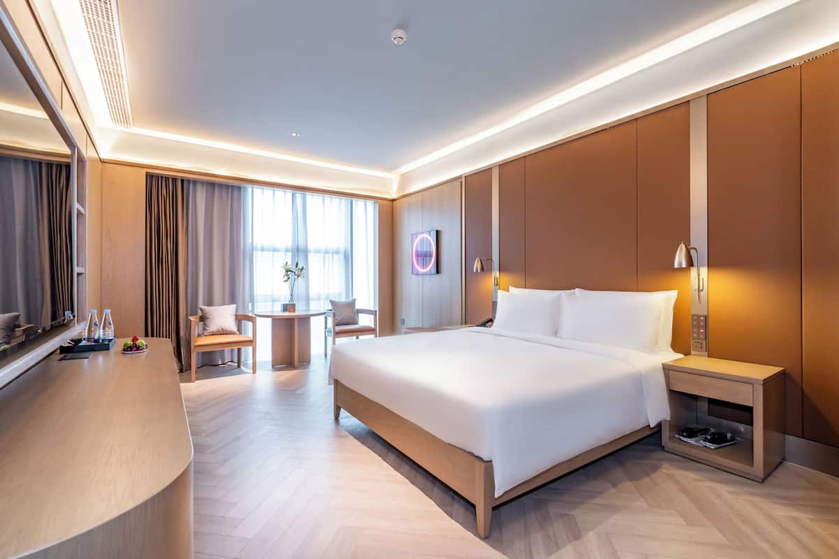 Quarto de hotel com uma cama grande, mesas de cabeceira, escrivaninha e uma cadeira.