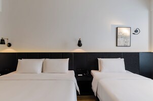 Quarto de hotel com duas camas, cabeceira escura, obra de arte na parede e mesa de cabeceira com telefone e controle remoto.