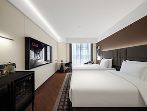 Quarto de hotel com uma cama grande, televisão, uma mesinha e um espaço para sentar.