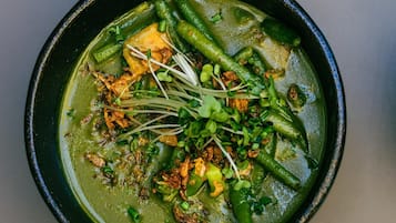 Uma frigideira com um prato de curry verde, contendo vagem, tofu e brotos.