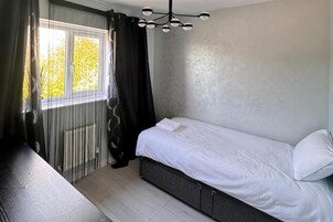 Quarto com uma cama de solteiro, radiador, janela com cortinas e luminária no teto.