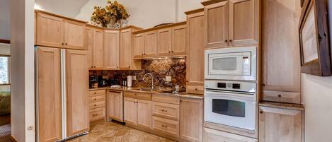 Uma cozinha com armários de madeira, painel de fundo de mármore, micro-ondas embutido e forno.