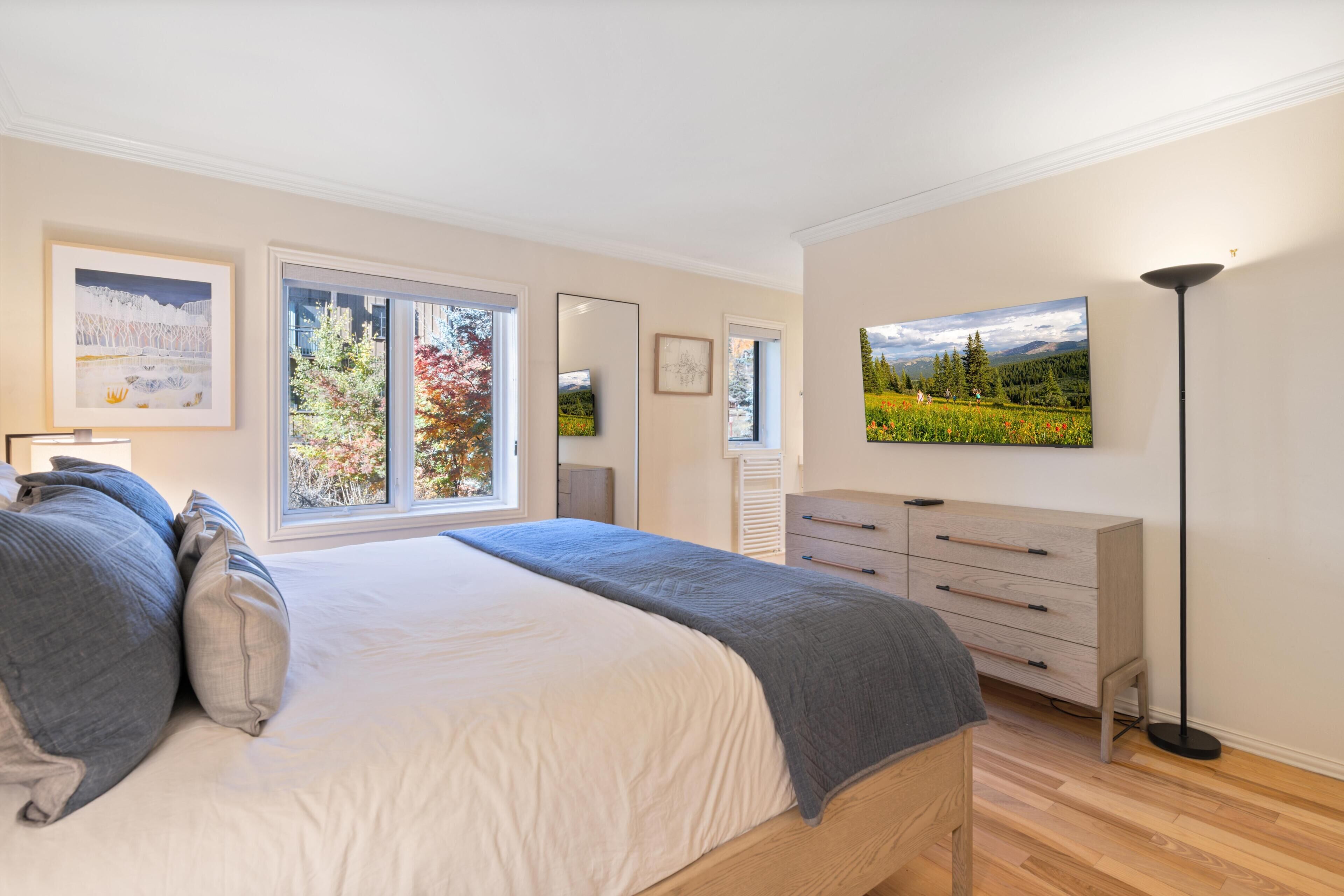 Um quarto com cama, cômoda, espelho e um quadro na parede.