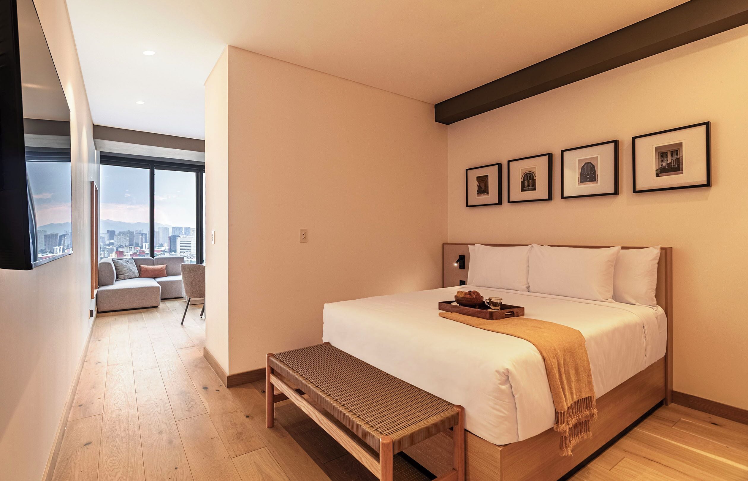 Quarto moderno com uma cama grande, um banco e vista para a cidade.