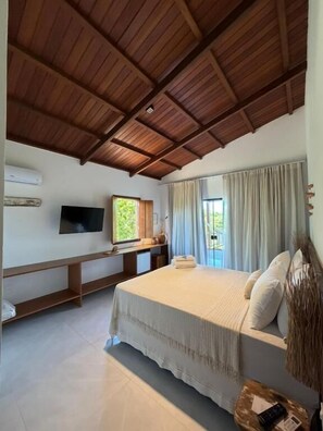 Quarto com teto de madeira, cama com roupa de cama branca, televisão na parede e janela com cortinas.