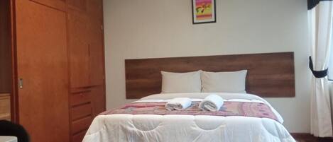 Quarto de hotel com uma cama, um guarda-roupa de madeira, um quadro na parede e uma janela com cortinas.