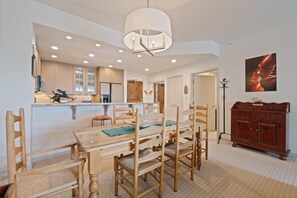 Uma cozinha moderna com armários de madeira, uma área de refeições com mesa de vidro e cadeiras de madeira, e um lustre.