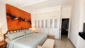 Quarto espaçoso com uma cama grande, um banco, uma TV e um guarda-roupa com portas venezianas.