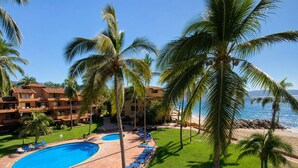 Um resort com piscina, palmeiras e vista para a praia.