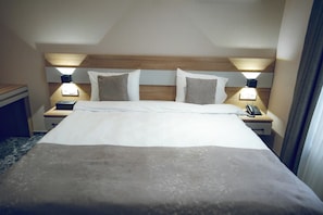 Quarto de hotel com uma cama grande, duas mesas de cabeceira com abajures e uma cabeceira de madeira.