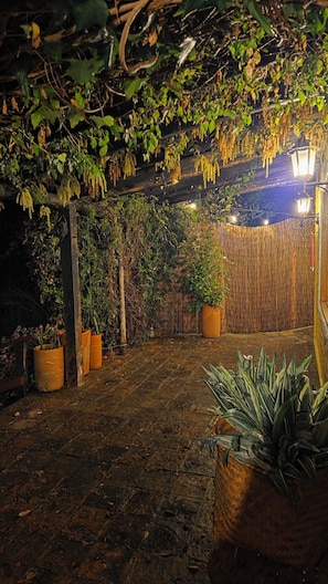 Área de terraço ao ar livre com pérgola de madeira, plantas em vasos e cerca de bambu.