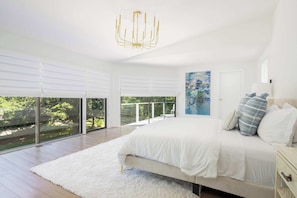 Quarto com cama grande, um lustre, um quadro e vista pela janela.