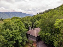 Uma casa rodeada por uma floresta densa, com uma montanha ao fundo.