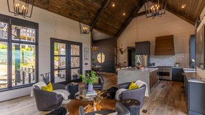 Um espaço amplo com teto alto, área de jantar com mesa de vidro e cozinha equipada com eletrodomésticos modernos.
