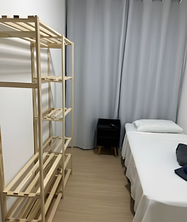 Quarto com beliche, estante de madeira, mesa preta pequena e cama branca com travesseiro.