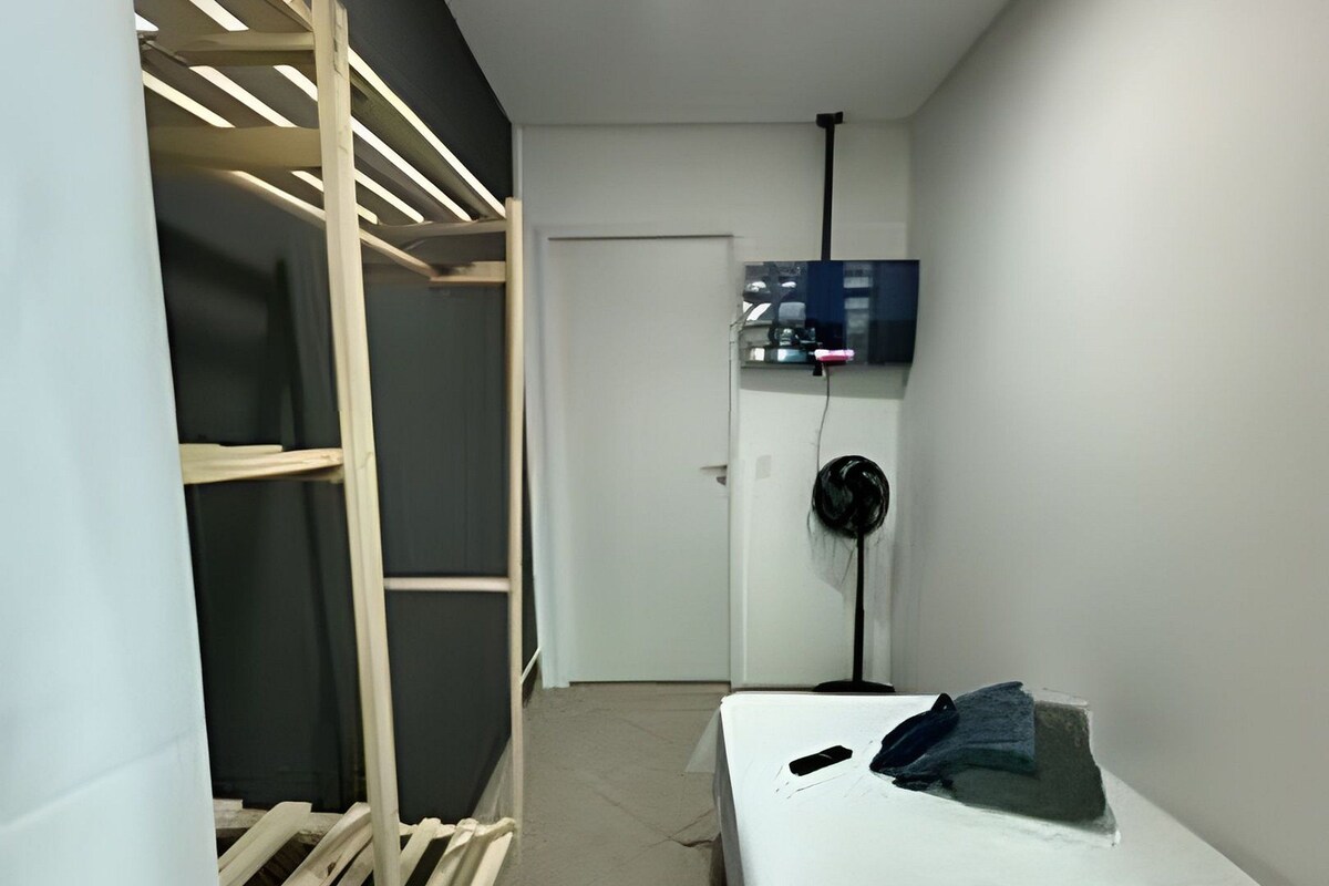 Quarto com cama, estante de madeira, porta branca e ventilador de teto.