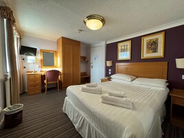 Quarto de hotel com cama, escrivaninha, cadeira, guarda-roupa e televisão.