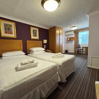 Quarto de hotel com duas camas, uma escrivaninha, uma cadeira e uma janela com cortinas.