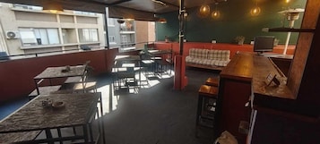 Restaurante com mesas, cadeiras, um sofá e luminárias pendentes.