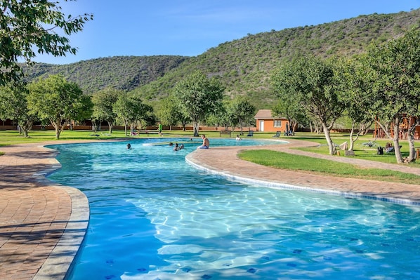 Piscina com água azul cristalina, rodeada por árvores e uma paisagem montanhosa.
