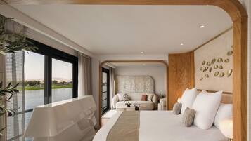Quarto de hotel moderno com uma cama grande, um sofá, vista para um corpo de água e uma parede decorativa.