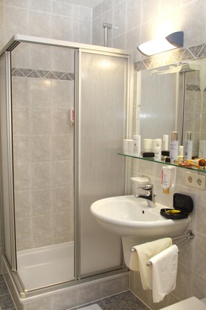Uma casa de banho com chuveiro em cabine de vidro, lavatório com artigos de higiene e espelho.