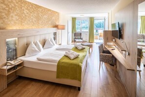 Quarto de hotel com cama, mesas de cabeceira, escrivaninha, cadeira, televisão e vista para o exterior.