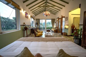 Um quarto amplo com uma cama grande, área de estar com sofá e poltronas, mesa de jantar e vista para o exterior.