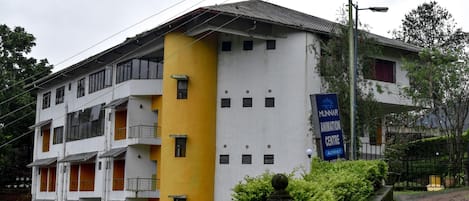 Um edifício de vários andares com fachada amarela e branca, varandas e uma placa com a inscrição 'Munnar Animation Centre'.