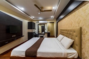 Quarto de hotel com cama, televisão, escrivaninha e ventilador de teto.
