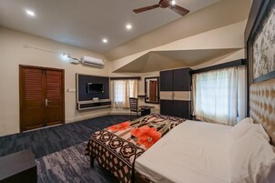 Quarto de hotel com cama, televisão, escrivaninha, cadeira, guarda-roupa e ar condicionado.