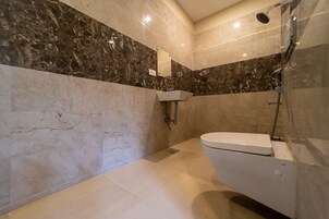 Uma casa de banho com parede de mármore, lavatório, sanita e chuveiro.