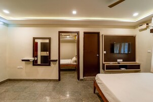 Quarto de hotel com cama, televisão, espelho e porta para um banheiro.