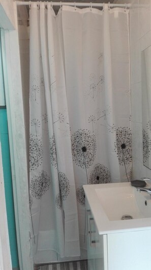 Casa de banho com cortina de chuveiro estampada com dentes-de-leão, uma pia branca e um espelho.