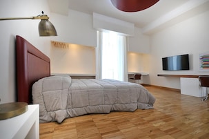 Quarto moderno com uma cama grande, televisão de tela plana e piso de madeira.