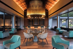 Um interior moderno com uma mesa redonda central rodeada por cadeiras, um espaço de bar e grandes janelas.