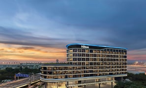 Um hotel moderno, com vários andares, fachada curva, grandes janelas e um letreiro chamativo com a inscrição 'Hilton'.